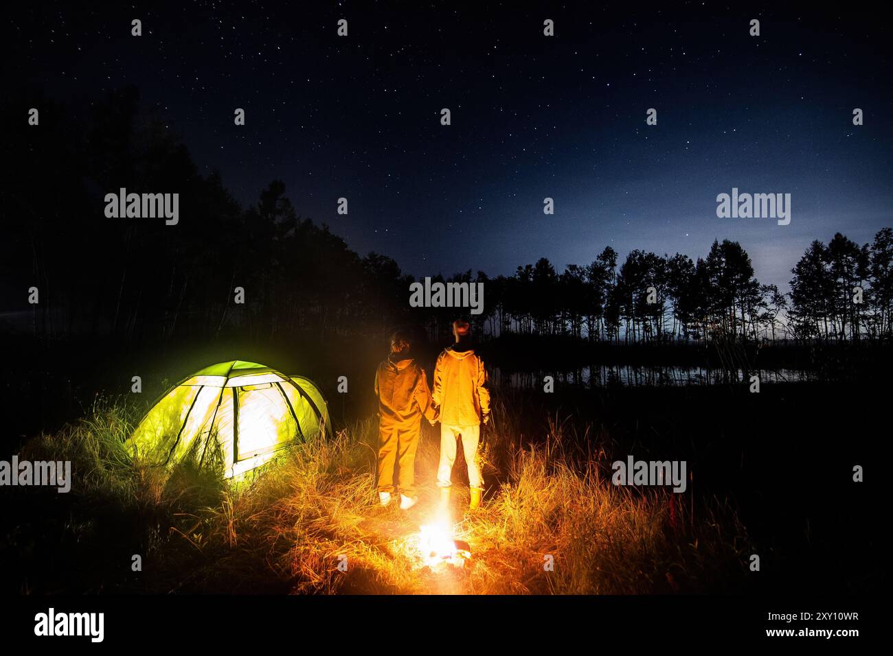 A couple of tourists standing at bonfire in their camp and looking to ...