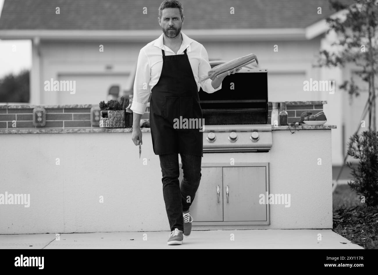 Handsome man in shirt and in cook apron preparing fish on barbecue ...