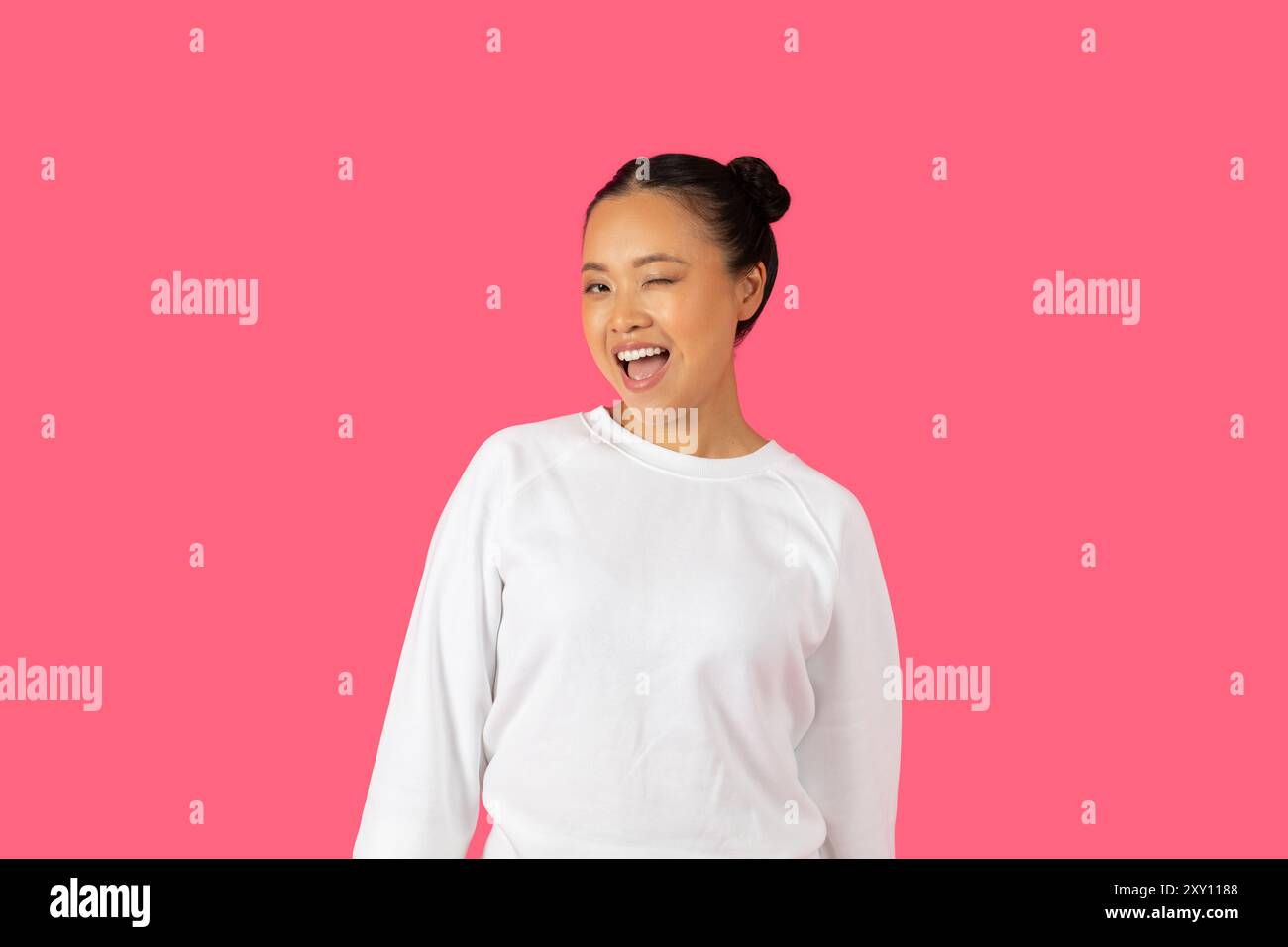 Young woman winks playfully against pink background in casual attire ...