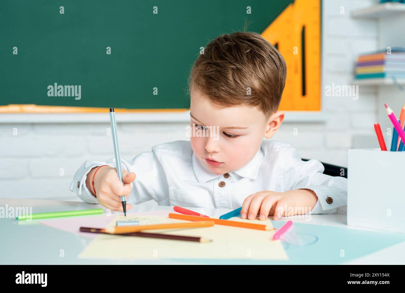 Cute child boy in classroom near blackboard desk. Kid is learning in ...