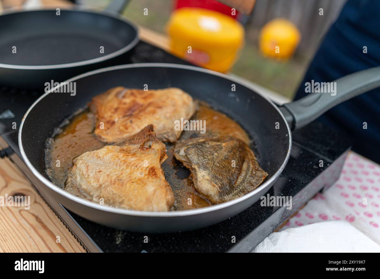 Three fish fillets sizzling in frying pans on a portable stove at an ...