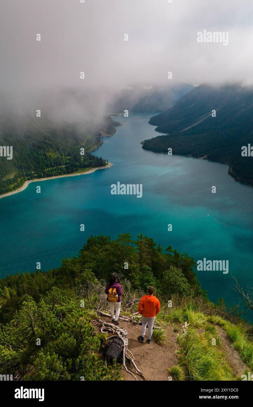 Two hikers admire the stunning turquoise waters of Plansee Lake ...