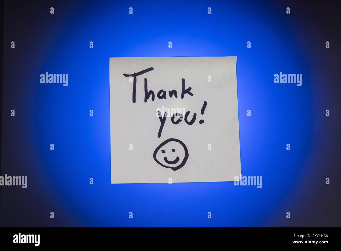 A thank you note with a smiley face drawn on it. The note is on a blue ...