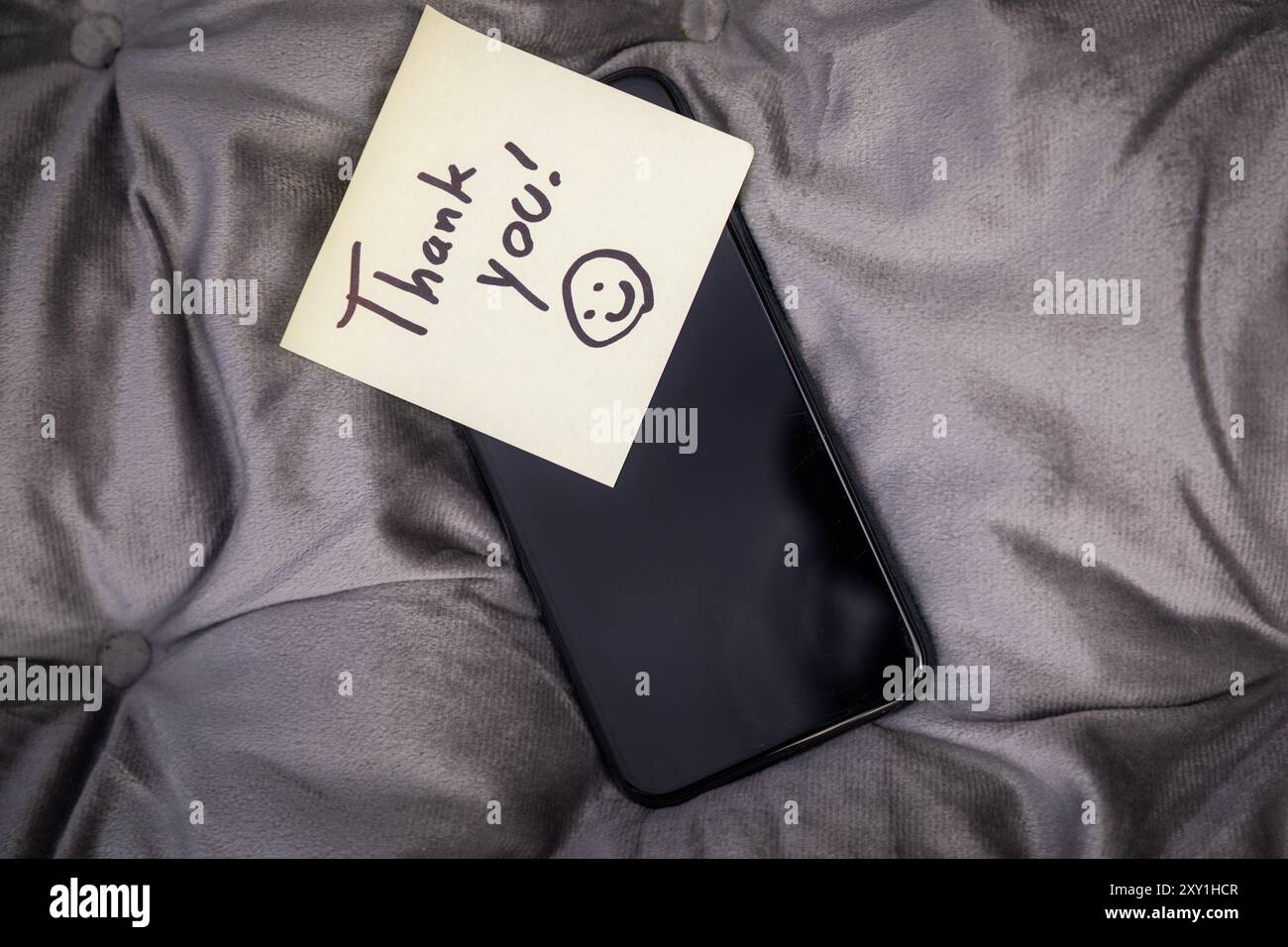 A cell phone with a note on it that says "Thank You"with a smiley face ...