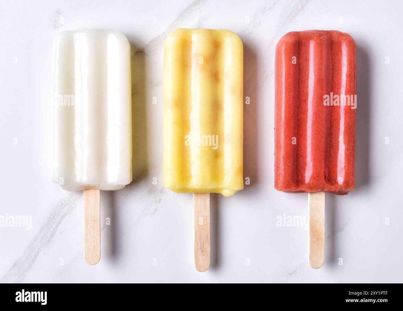 top view of three different ice pops on a marble counter top. Red ...