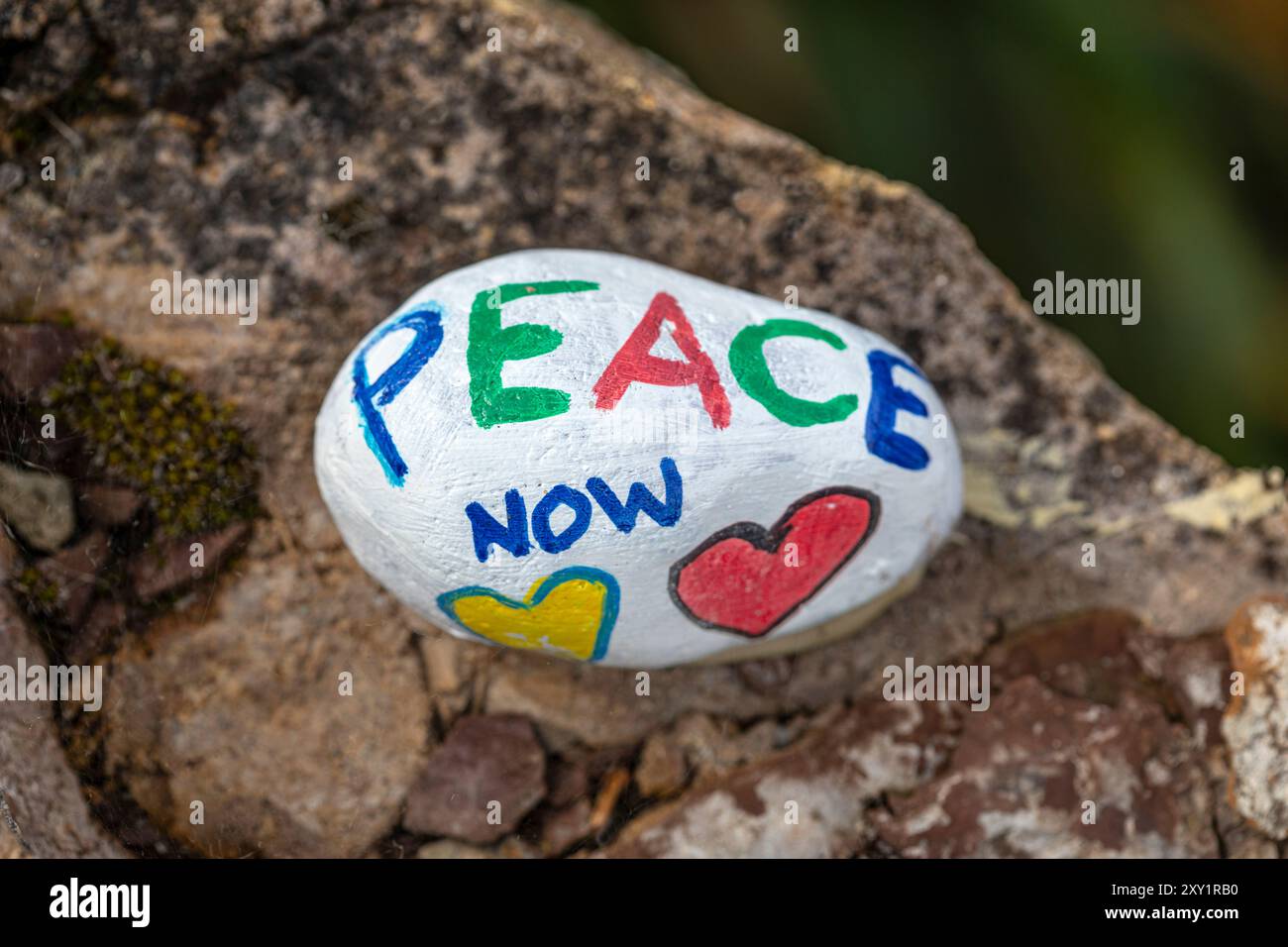 A small white pebble with Peace Now and two hearts painted on it Stock ...