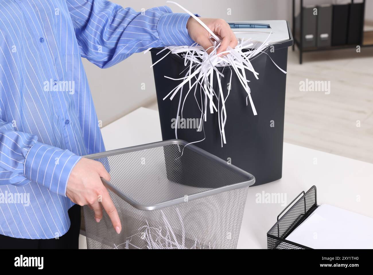 Woman putting shredded paper strips into trash bin at white table in ...