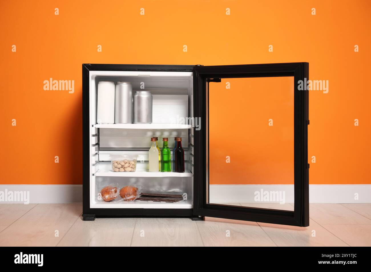 Mini refrigerator with different drinks and snacks near orange wall ...