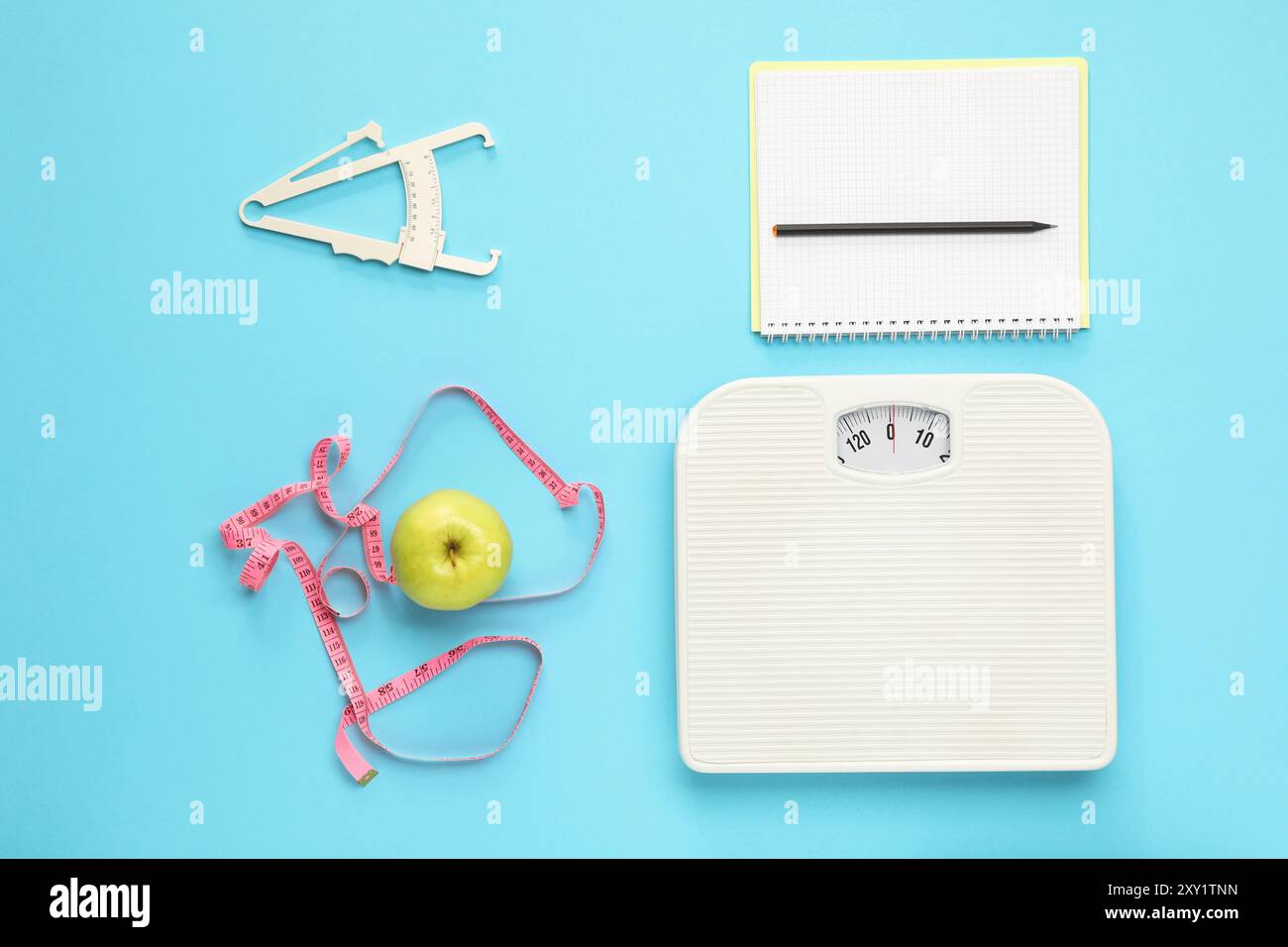 Flat lay composition with body fat caliper and scale on light blue ...