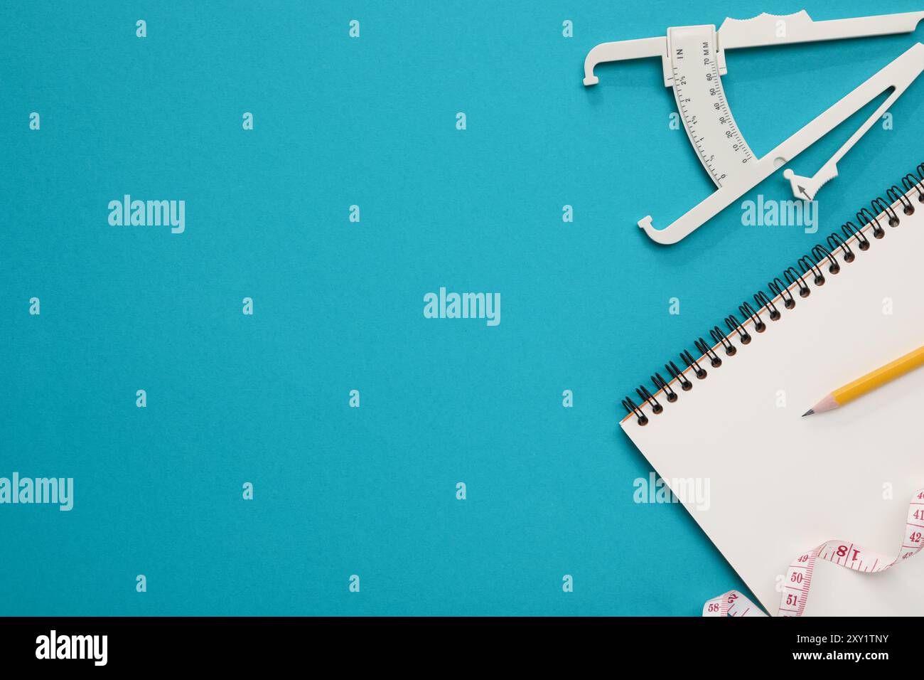 Body fat caliper, measuring tape, notebook and pencil on light blue ...