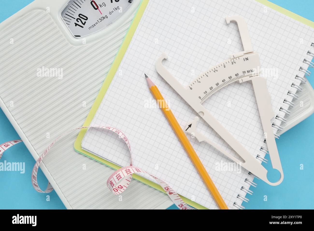 Body fat caliper, measuring tape, scale and notebook on light blue ...