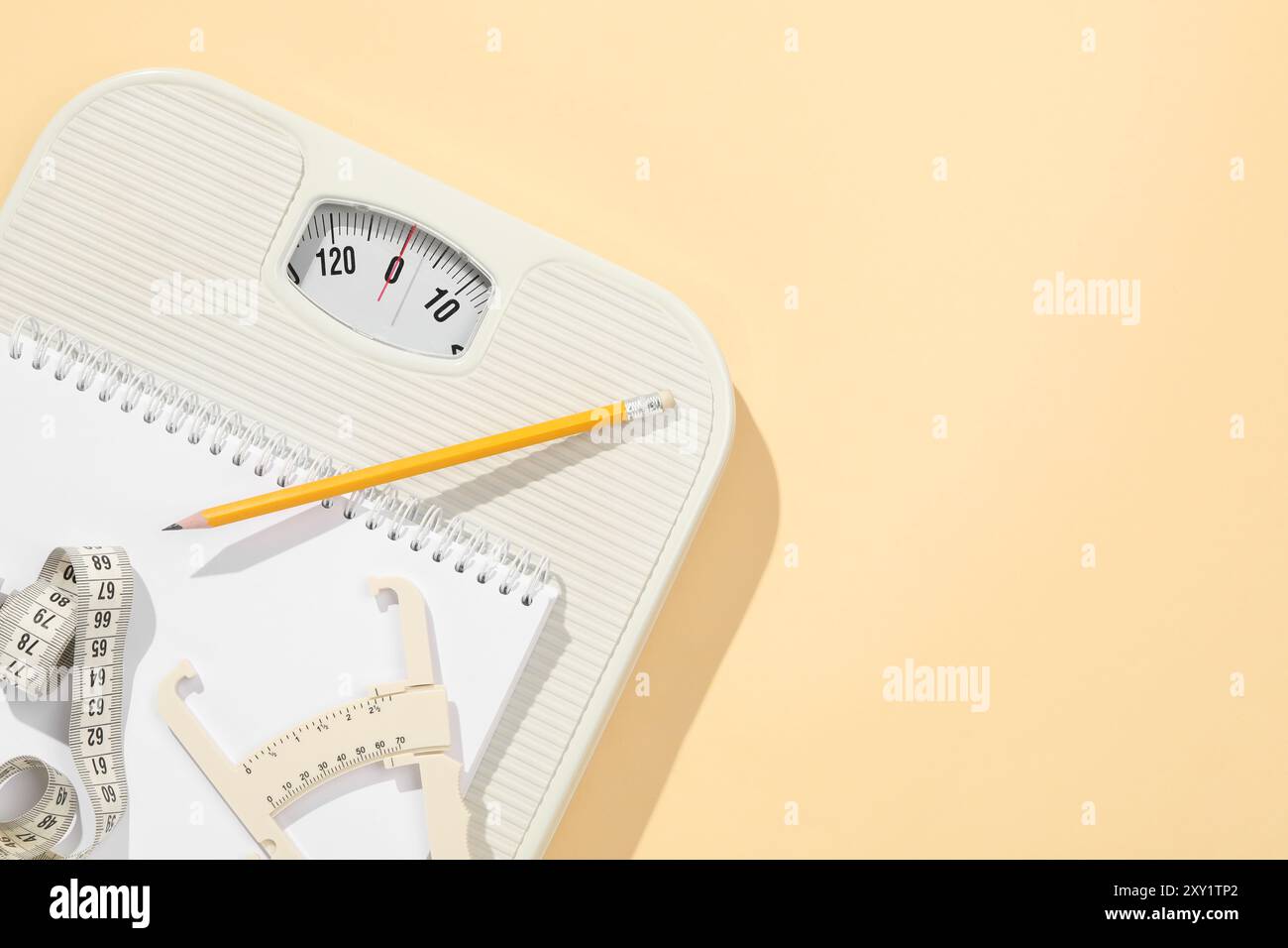 Body fat caliper, measuring tape, scale, pencil and notebook on beige ...