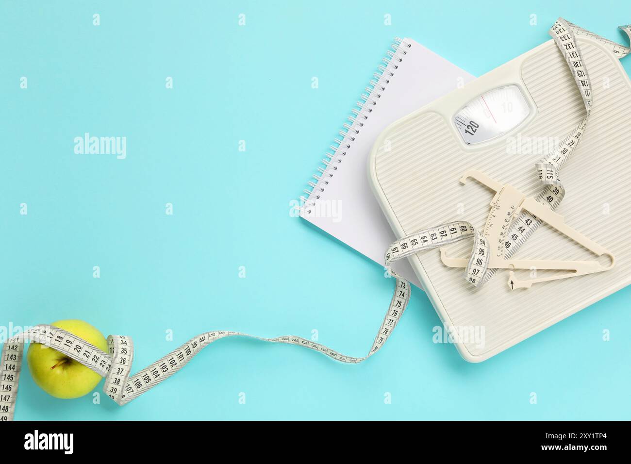 Body fat caliper, measuring tape, apple and notebook on light blue ...