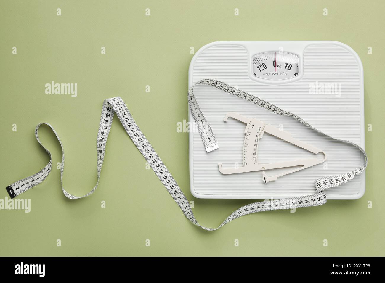 Body fat caliper, measuring tape and scale on light green background ...