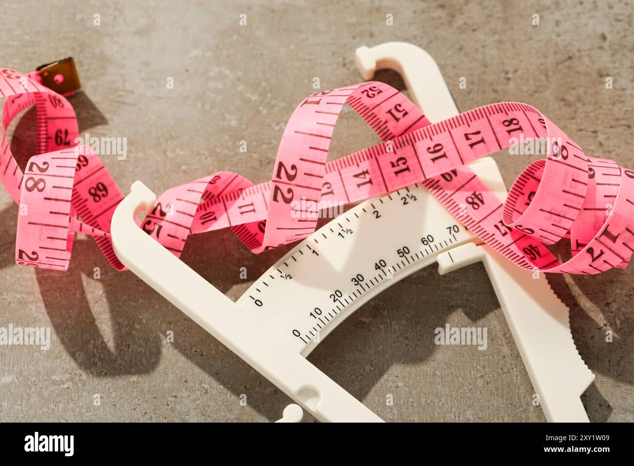 Plastic body fat caliper and measuring tape on grey table, closeup ...