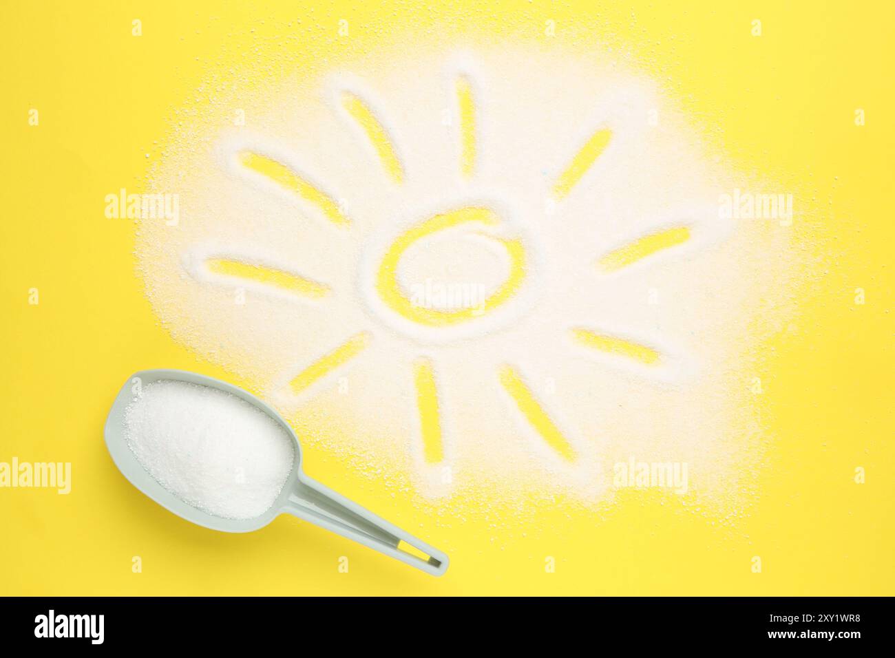 Measuring scoop and sun made with laundry powder on yellow background ...