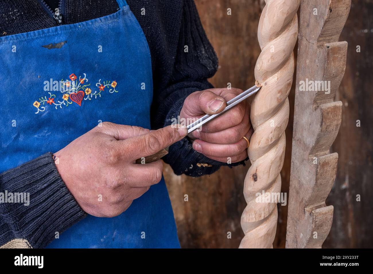craftsman in an embroidered blue apron works a twisted wooden column ...