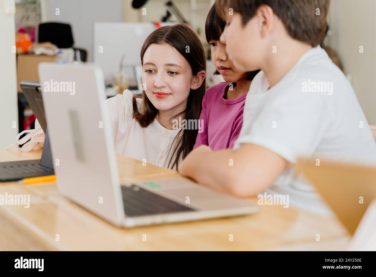 Young teacher guides diverse students with digital devices in modern ...