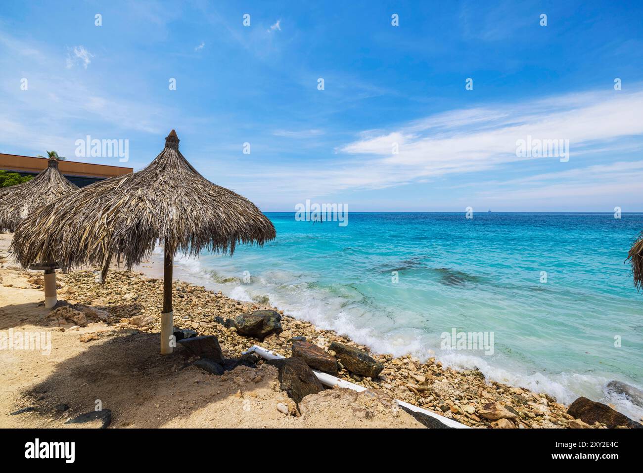 Rocky beach on Aruba with blue Caribbean water and palm leaf umbrellas ...