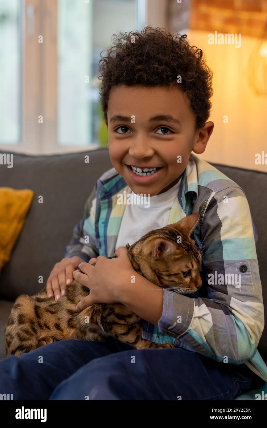 Happy dark-skinned boy playing with a cat and looking Stock Photo - Alamy