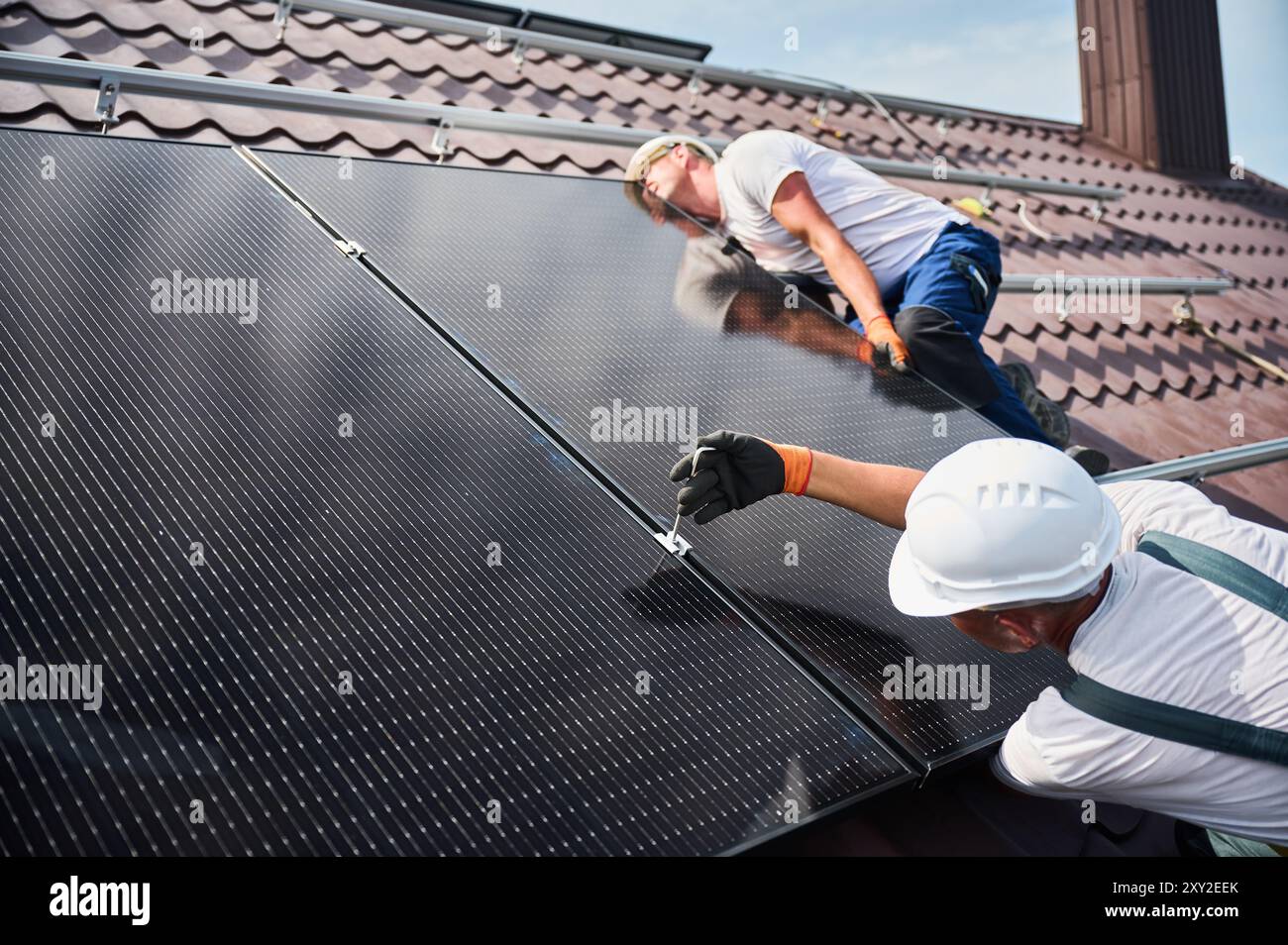 Workers building photovoltaic solar panel system on rooftop of house. Close up of men ...
