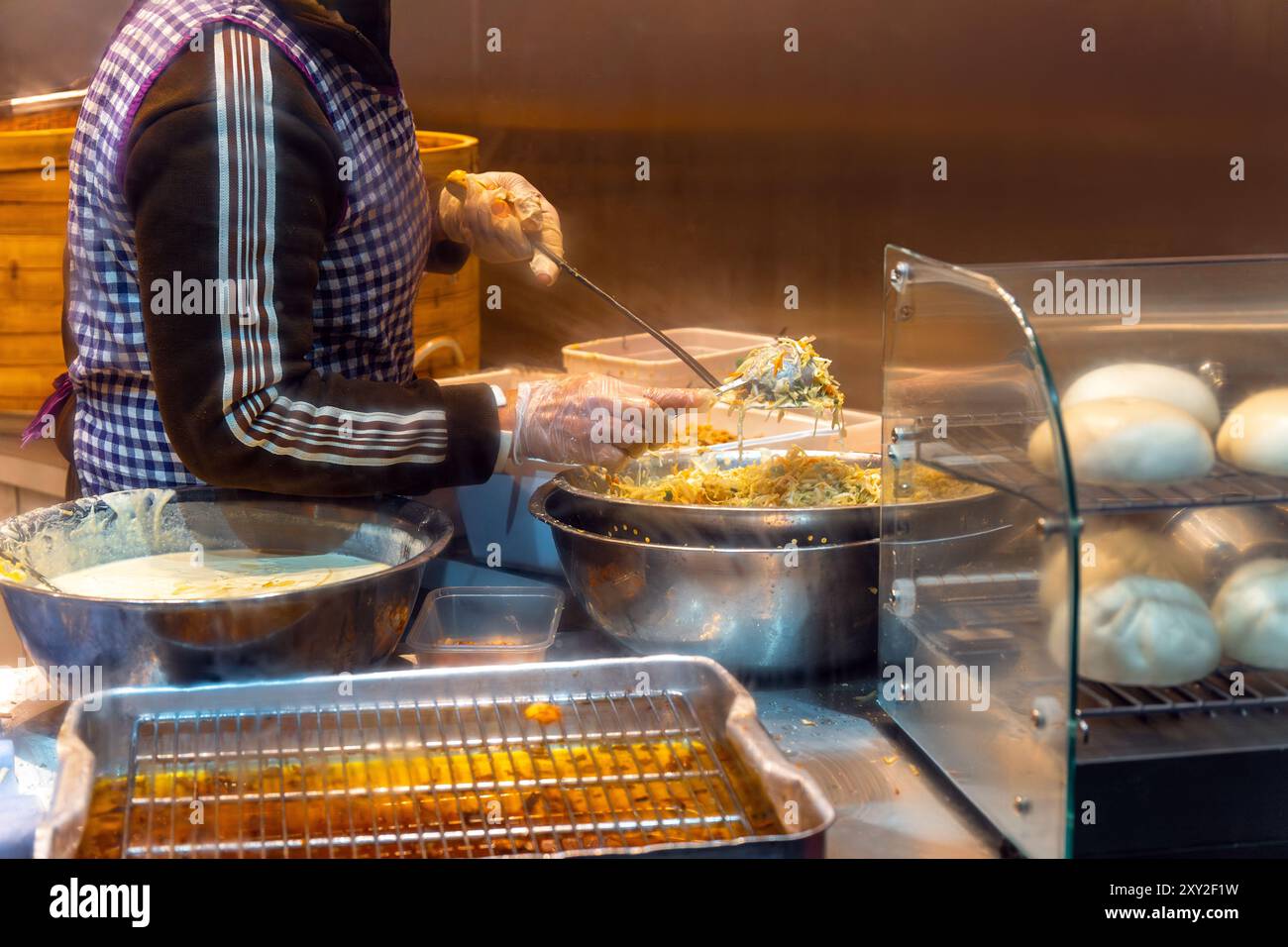 Chinese chef in apron and plastic gloves cooking dough and ingredients ...