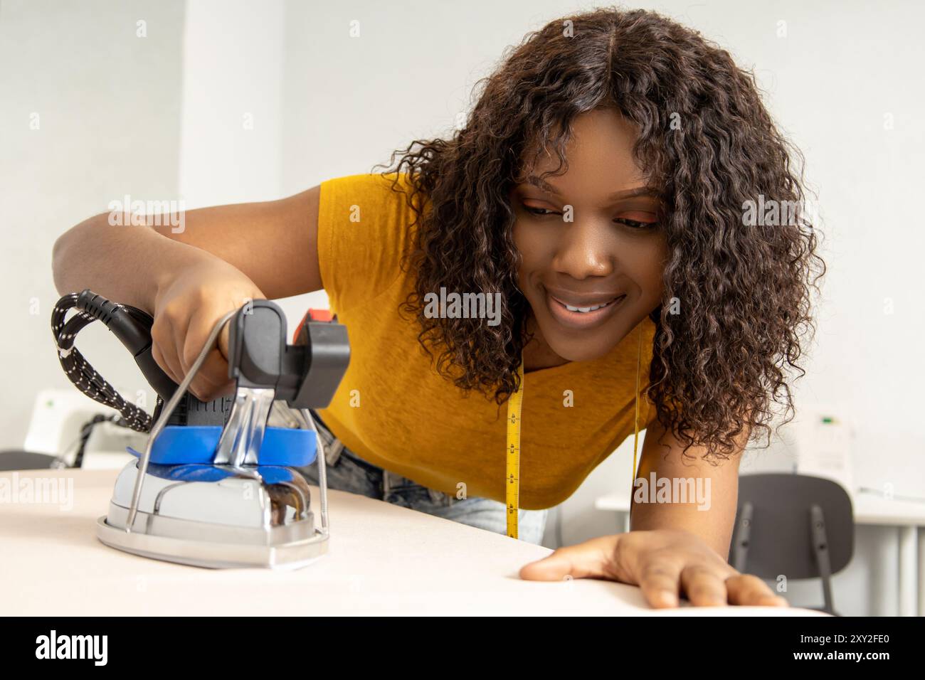 Smiling woman seamstress ironing textile for sewing dress at tailoring ...