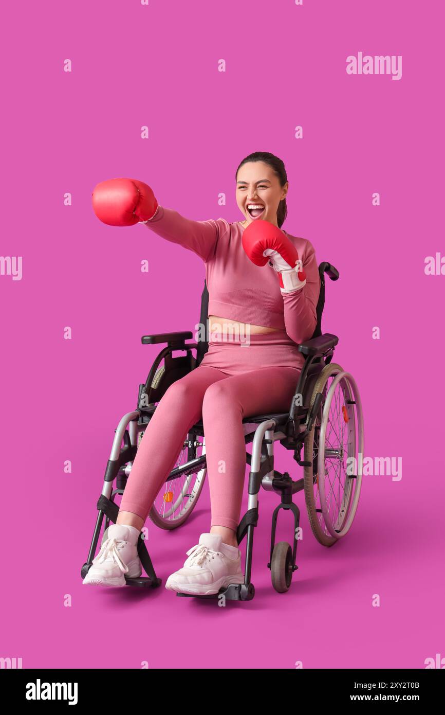 Sporty young woman in wheelchair with boxing gloves on purple ...