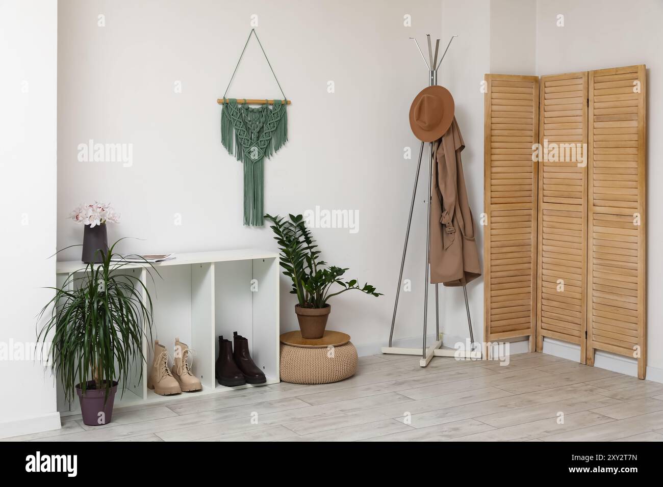 Interior of stylish hall with rack of clothes and houseplant near white ...