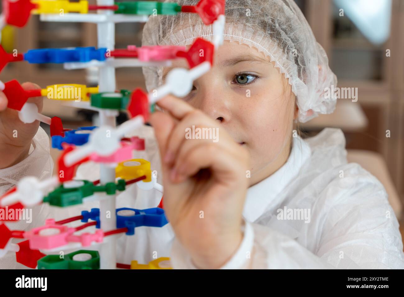 Schoolgirl studying DNA model, in white coat in school classroom. High ...
