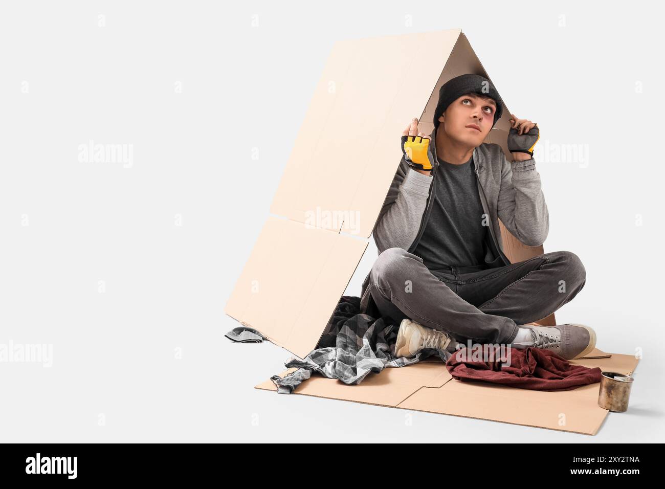 Young homeless man with cardboard sitting on light background Stock ...