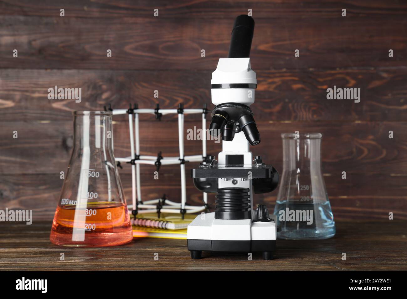 Modern microscope with chemical flasks and molecular model on table ...