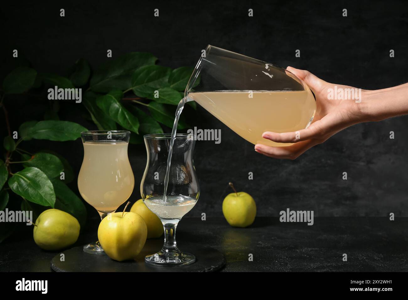 Woman pouring fresh apple kvass from jug into glass on black background Stock Photo - Alamy