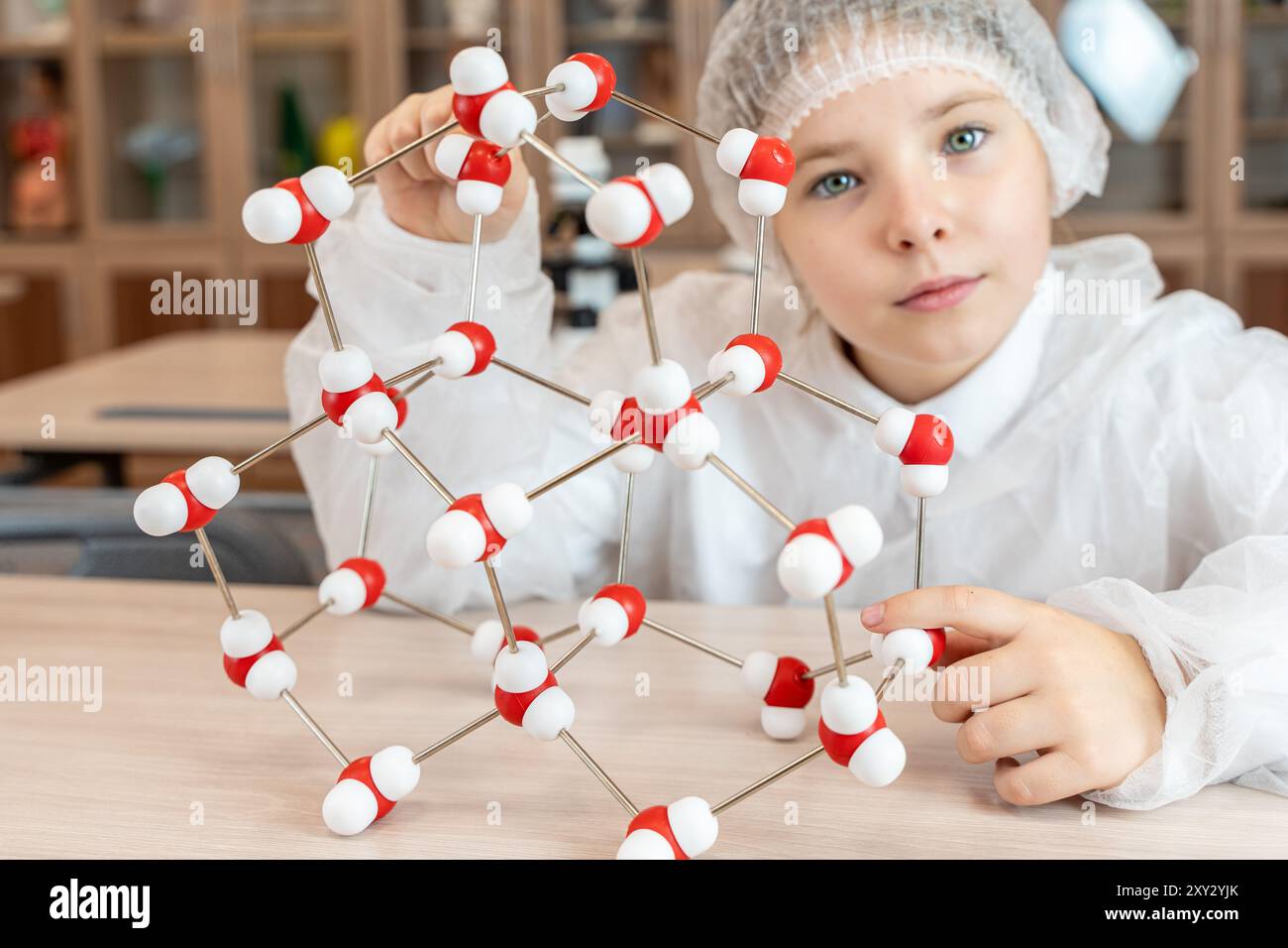 A schoolgirl in a white coat demonstrates an atomic model of a molecule ...