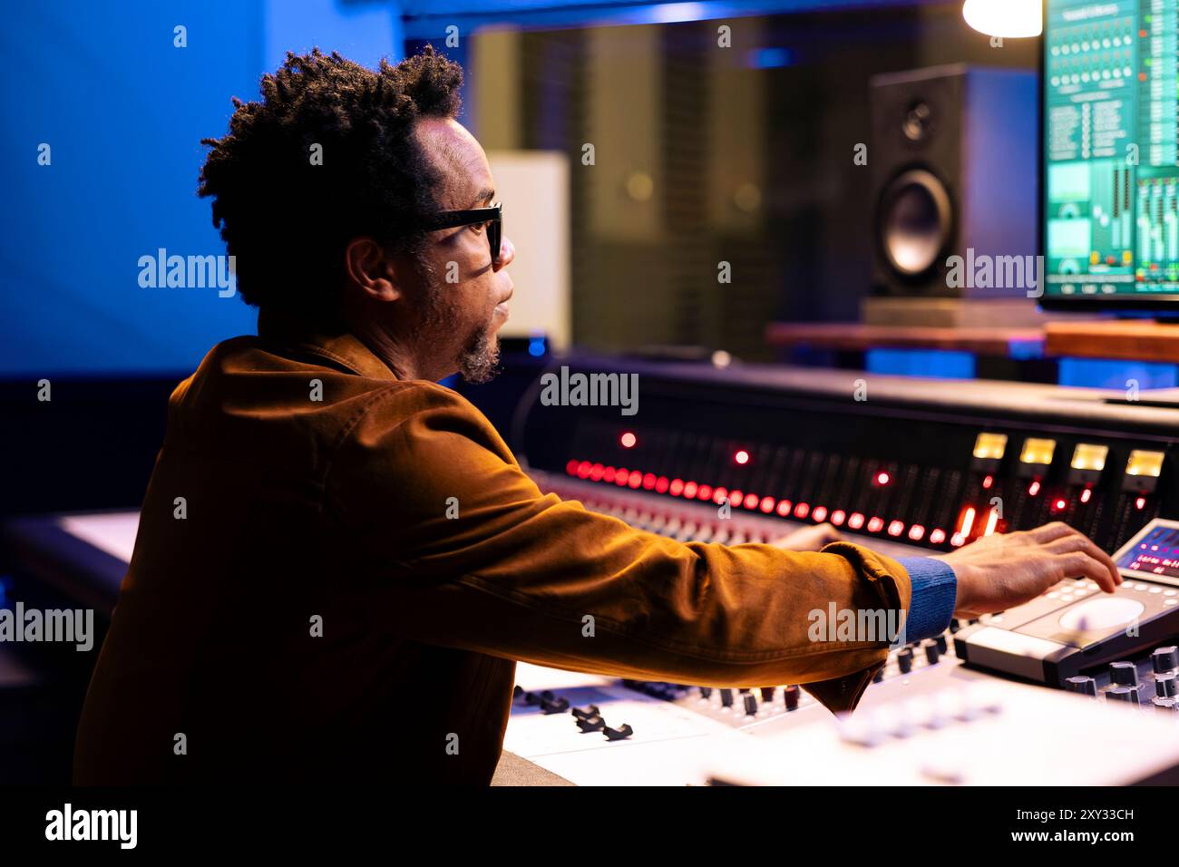 African american record producer adjusting sound settings on control board desk, editing tunes ...