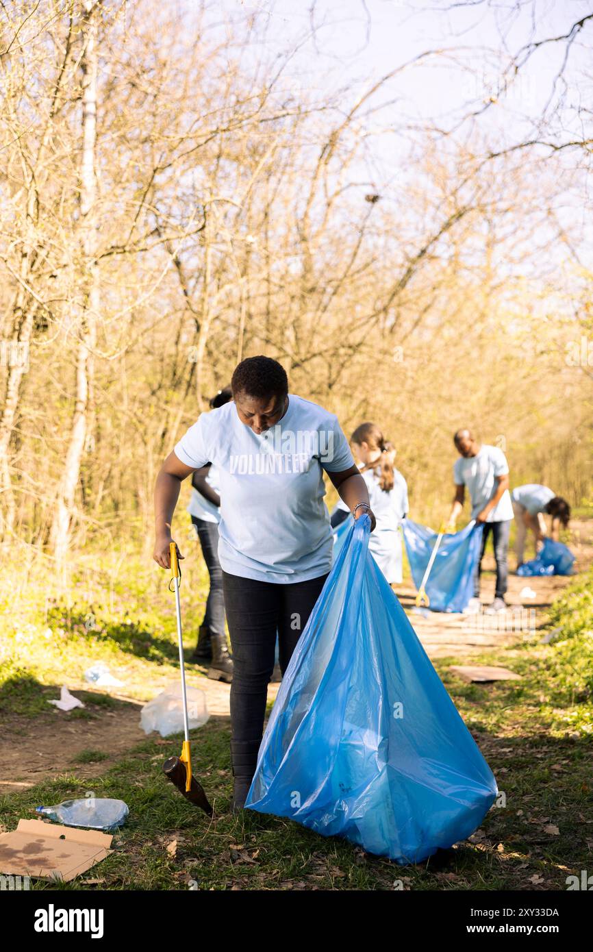 Woman activist grabbing garbage with a claw tool in the forest ...