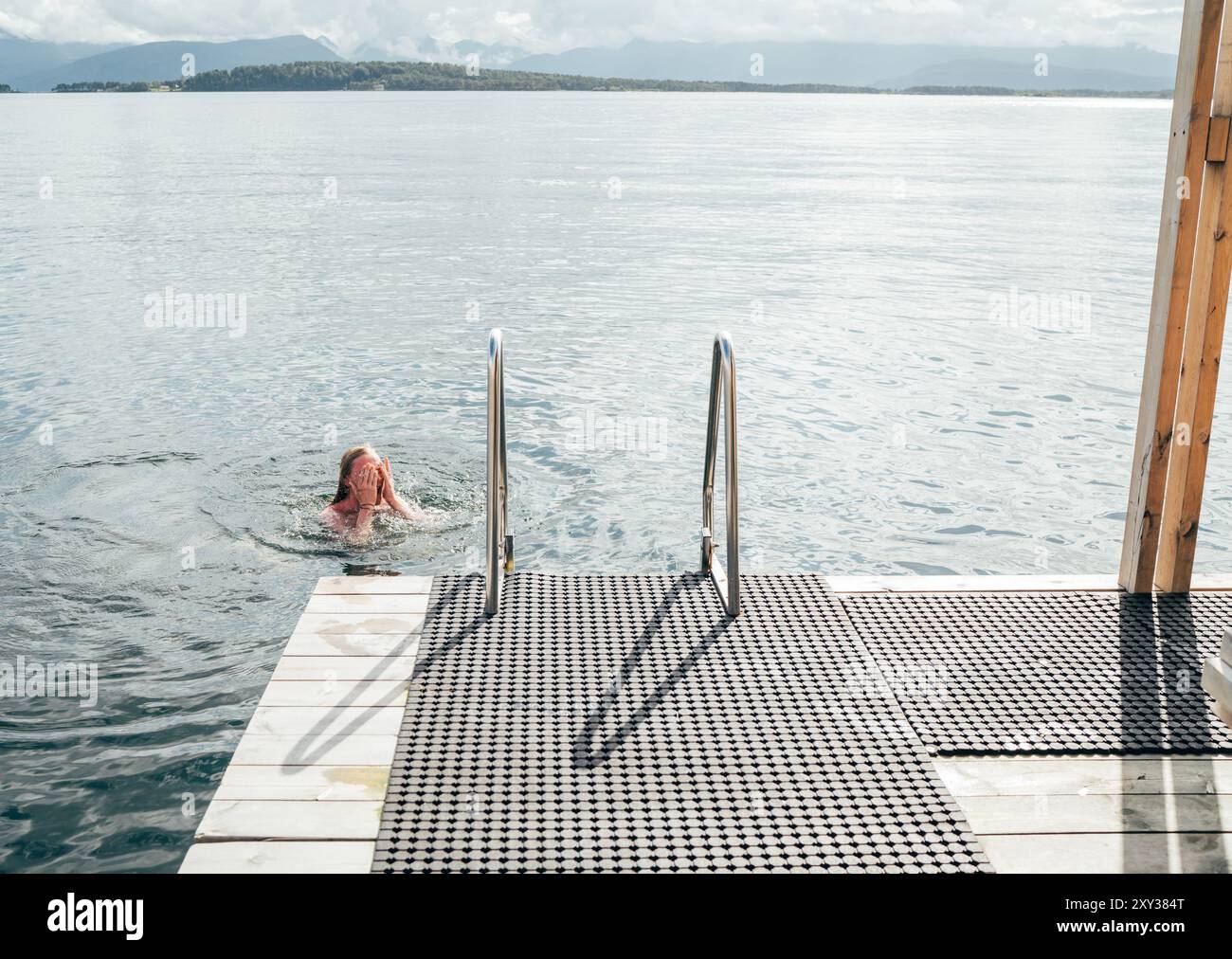 Swimming teen boy into the cold Fjord water next to Scandinavian ...