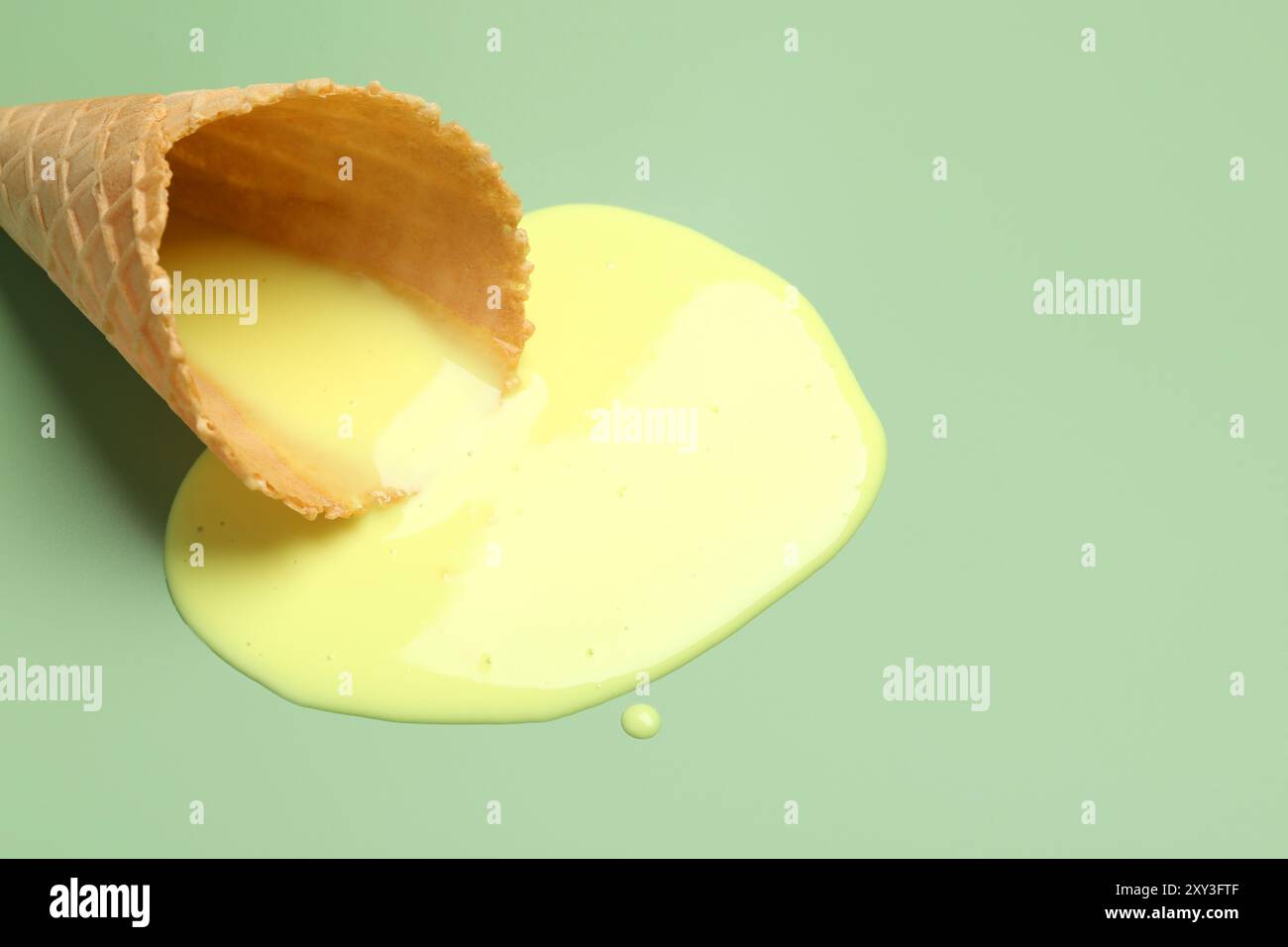 Melted ice cream and wafer cone on light green background, closeup ...