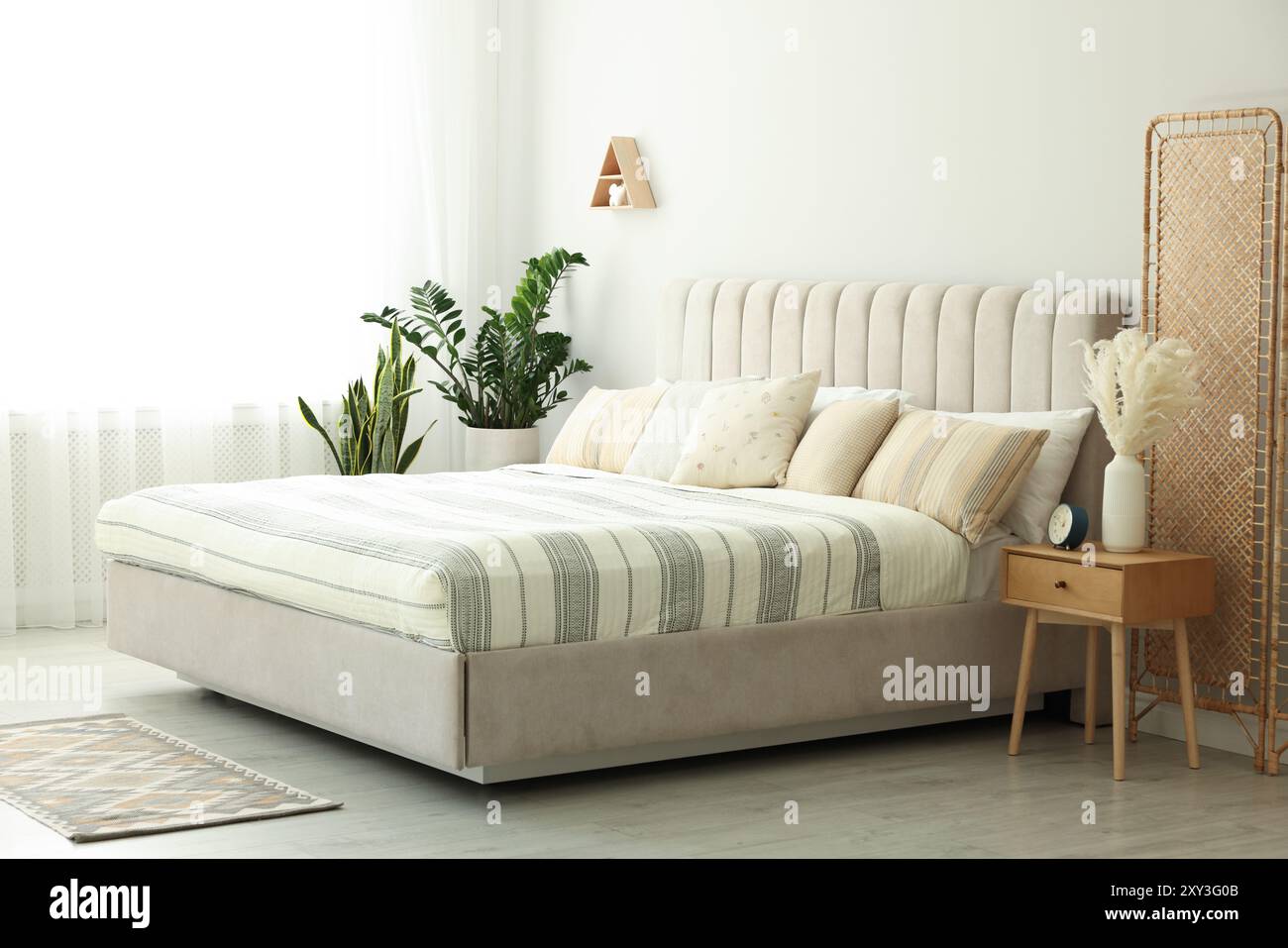 Large bed, houseplants and bedside table in stylish room Stock Photo ...