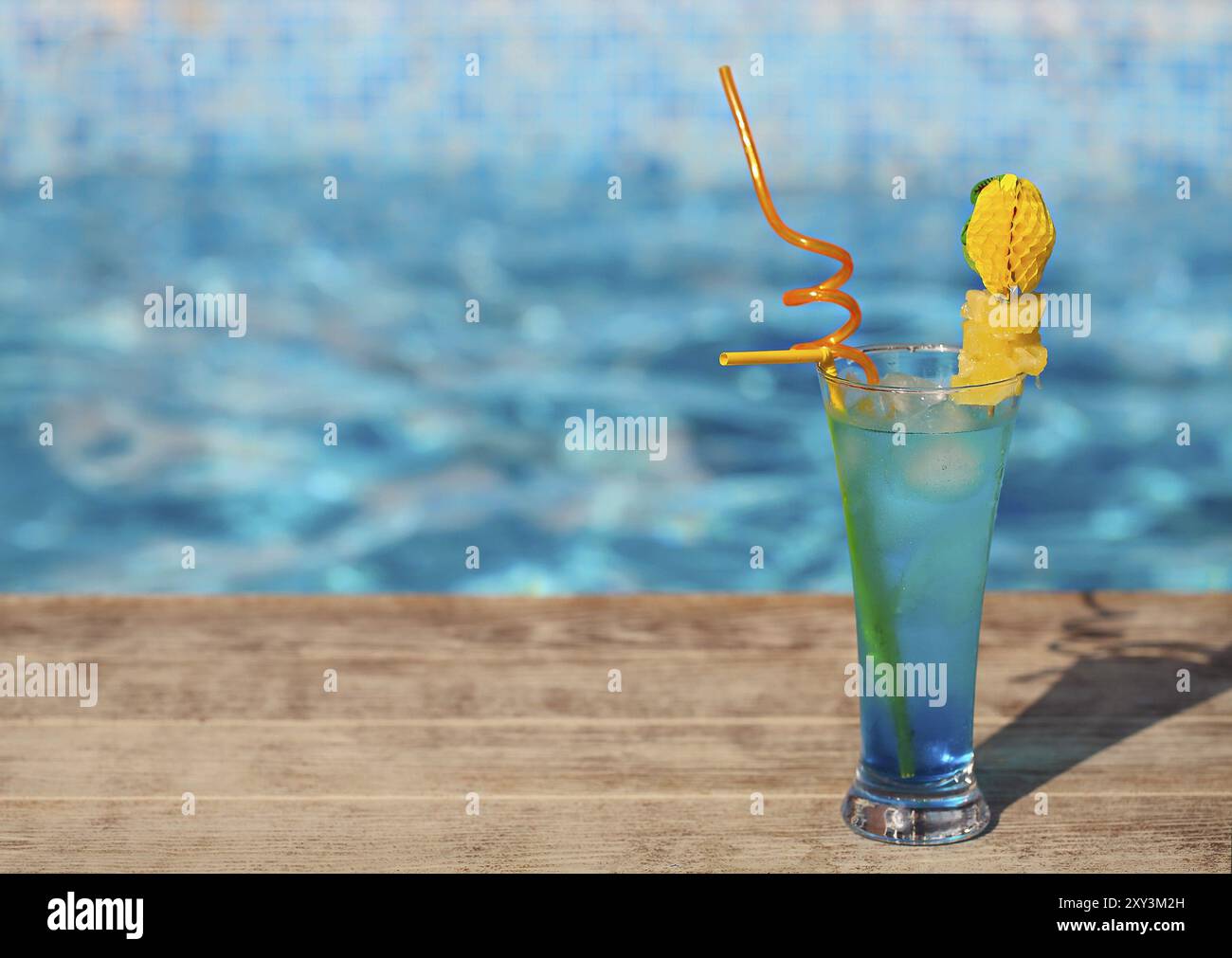 Glass with a bright blue lagoon cocktail on the table by the pool ...