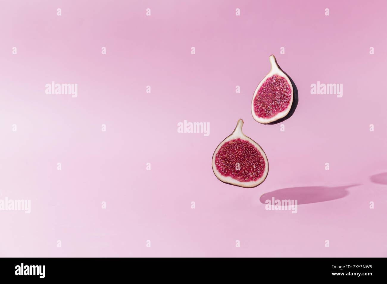 Fresh tasty fig fruit halves levitation with shadow on pink background ...