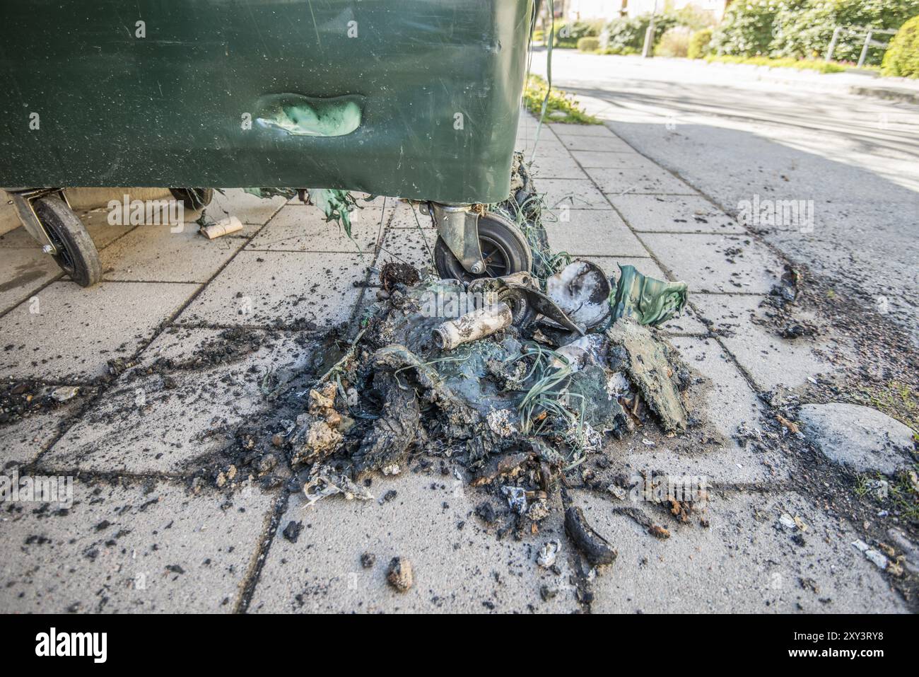 A plastic trash bin has burnt and The melted remains are on the ground ...