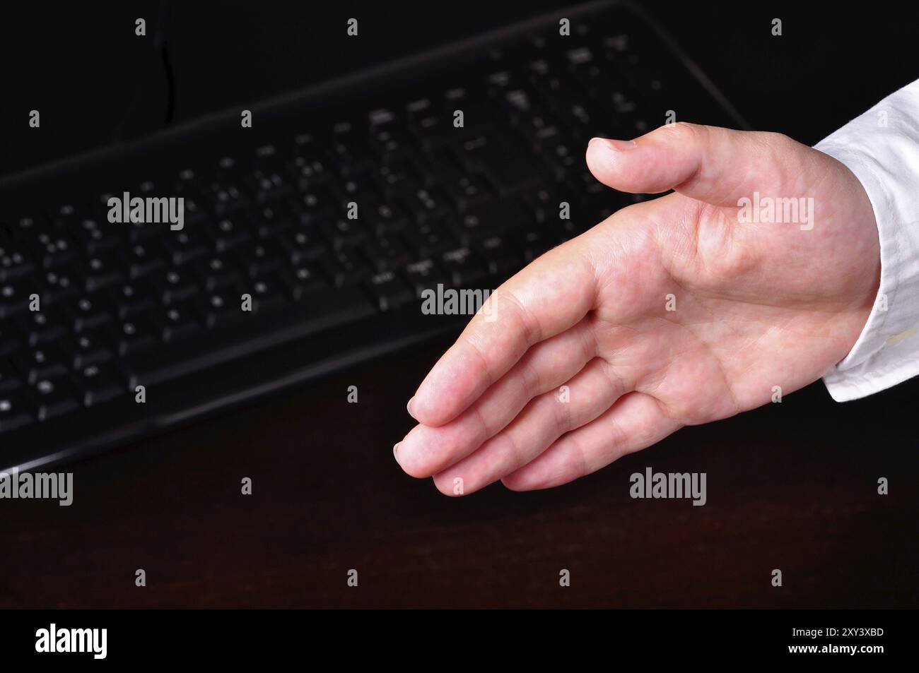 Hand ready for an handshake next do a computer keyboard on a dark table ...