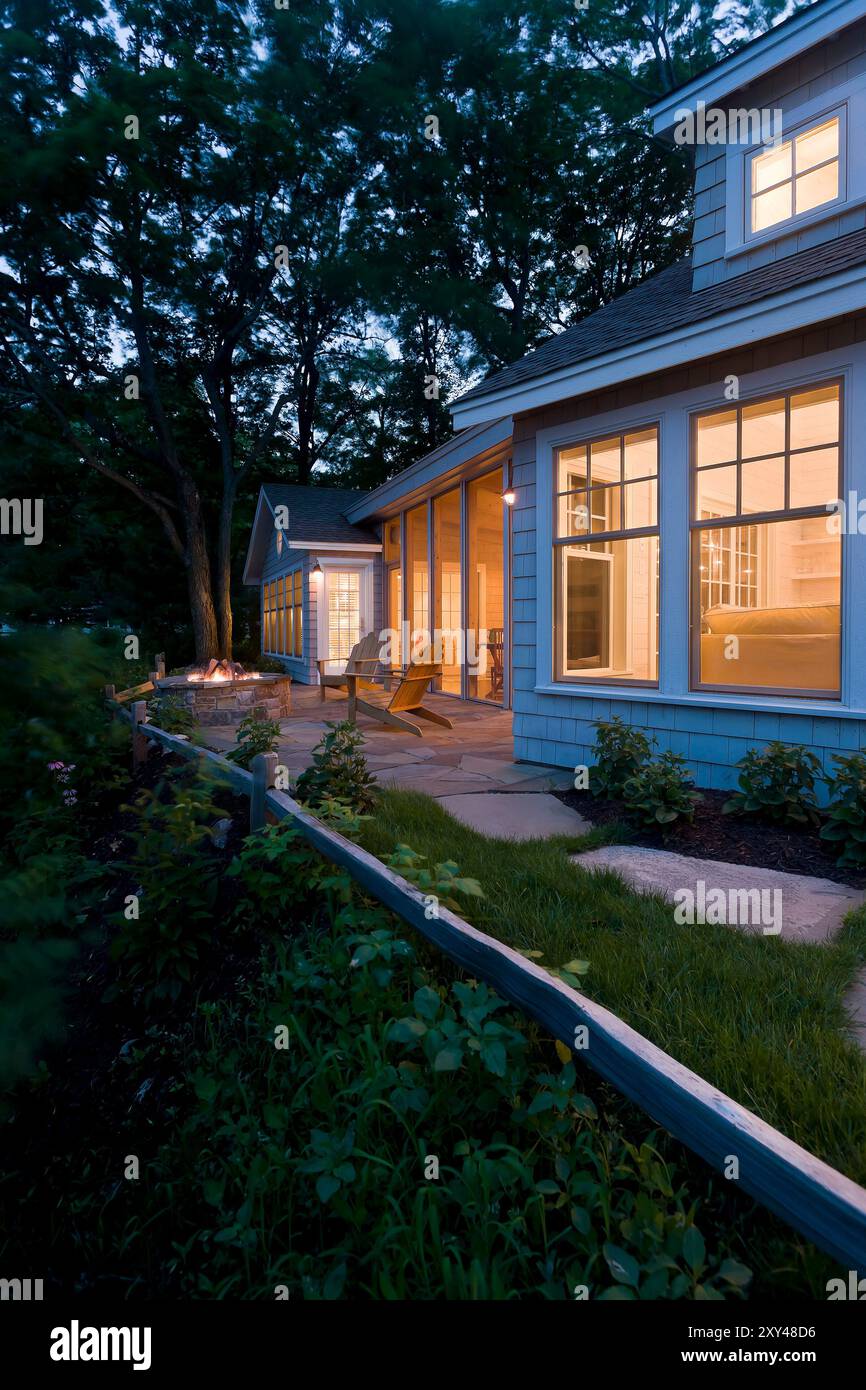 Cottage surrounded by trees lit up at night with patio area in front ...