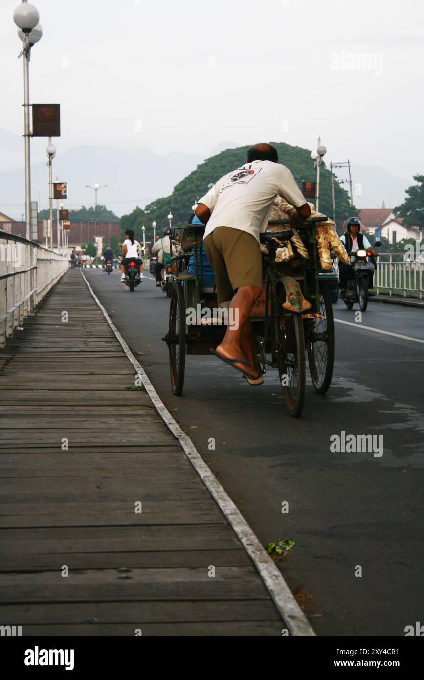 Rear view of a pedicab driver pedaling his trishaw on the old bridge ...