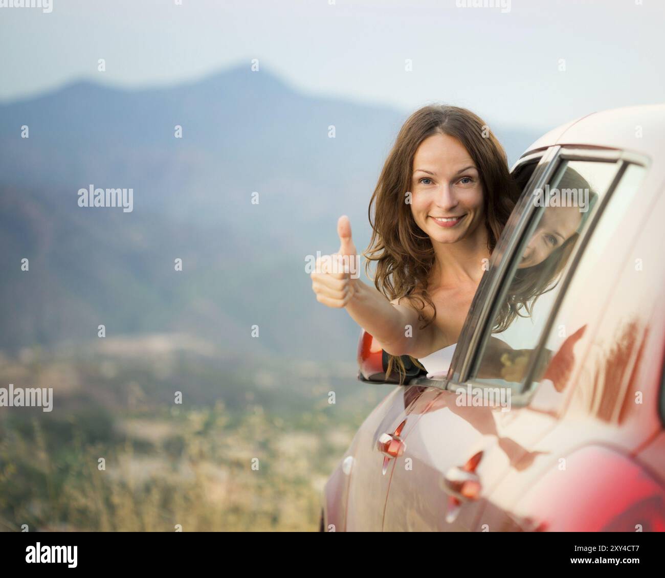 Happy driver woman showing thumb up sign against mountains background ...