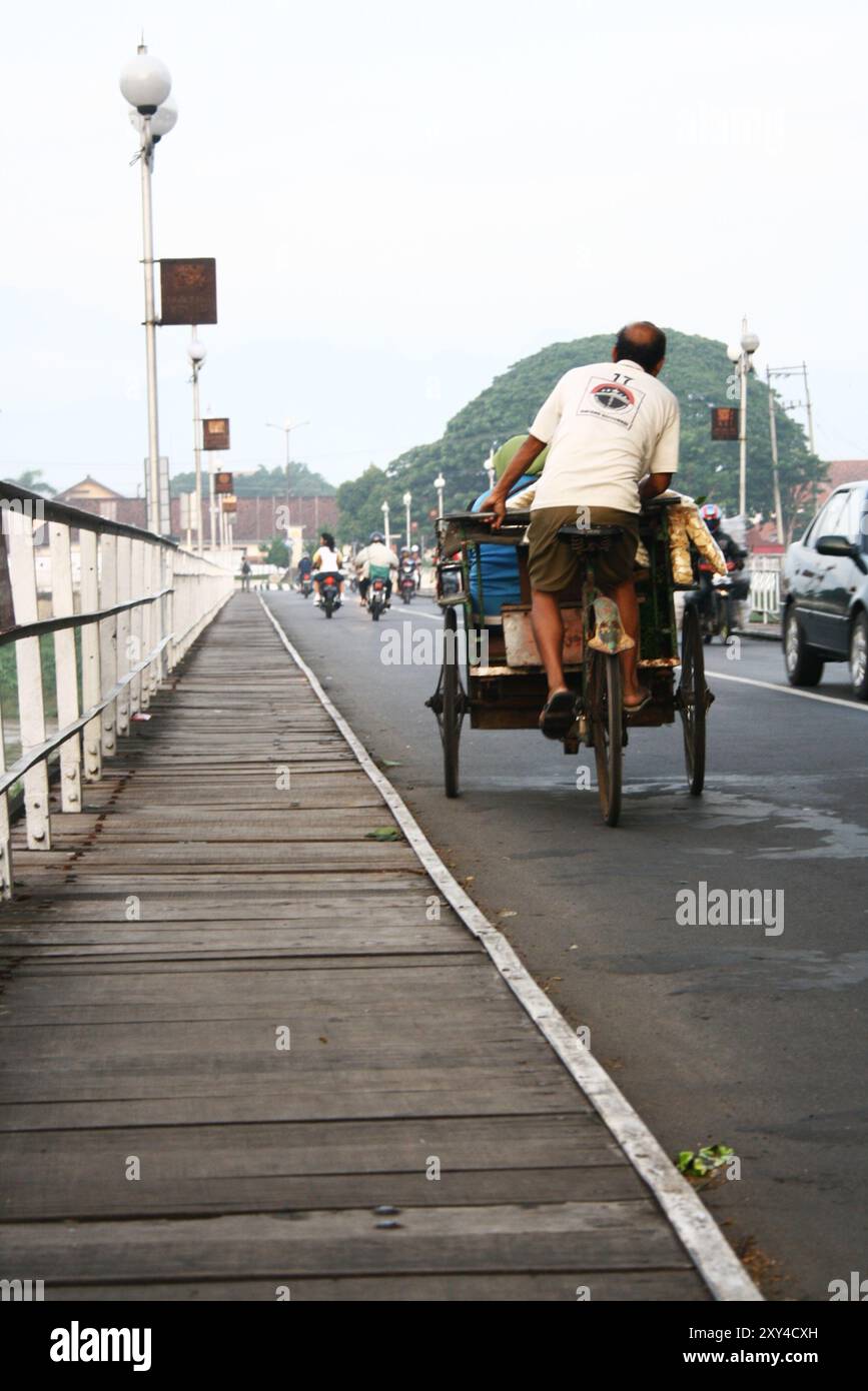 Rear view of a pedicab driver pedaling his trishaw on the old bridge ...