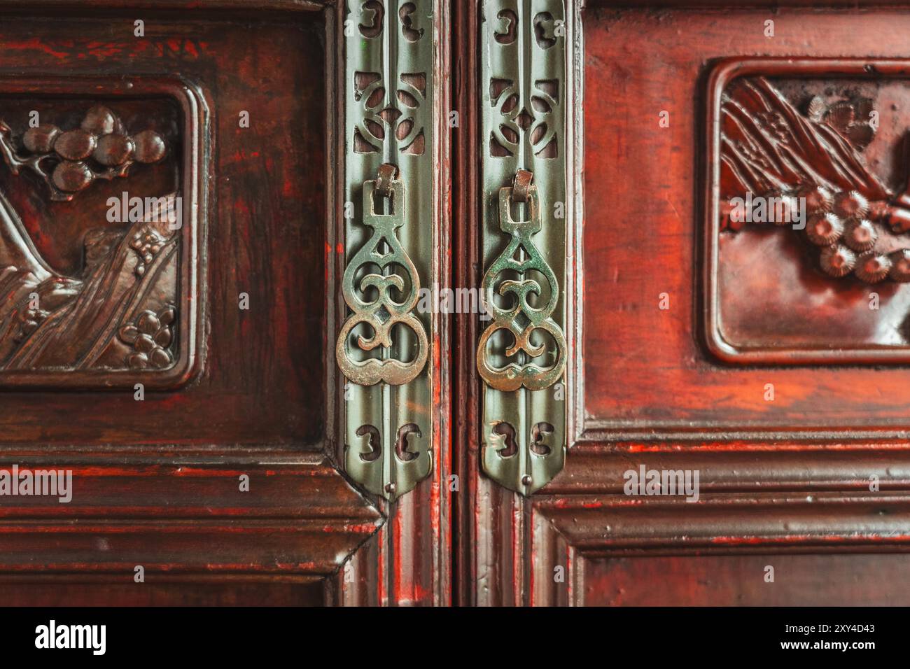 A close-up of two ornate metal handles set into a wooden cabinet with ...