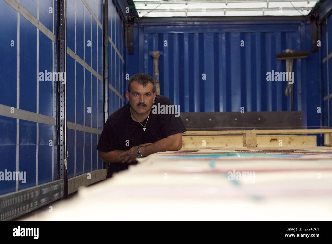 A lorry driver stands in a lorry trailer and leans against the load ...