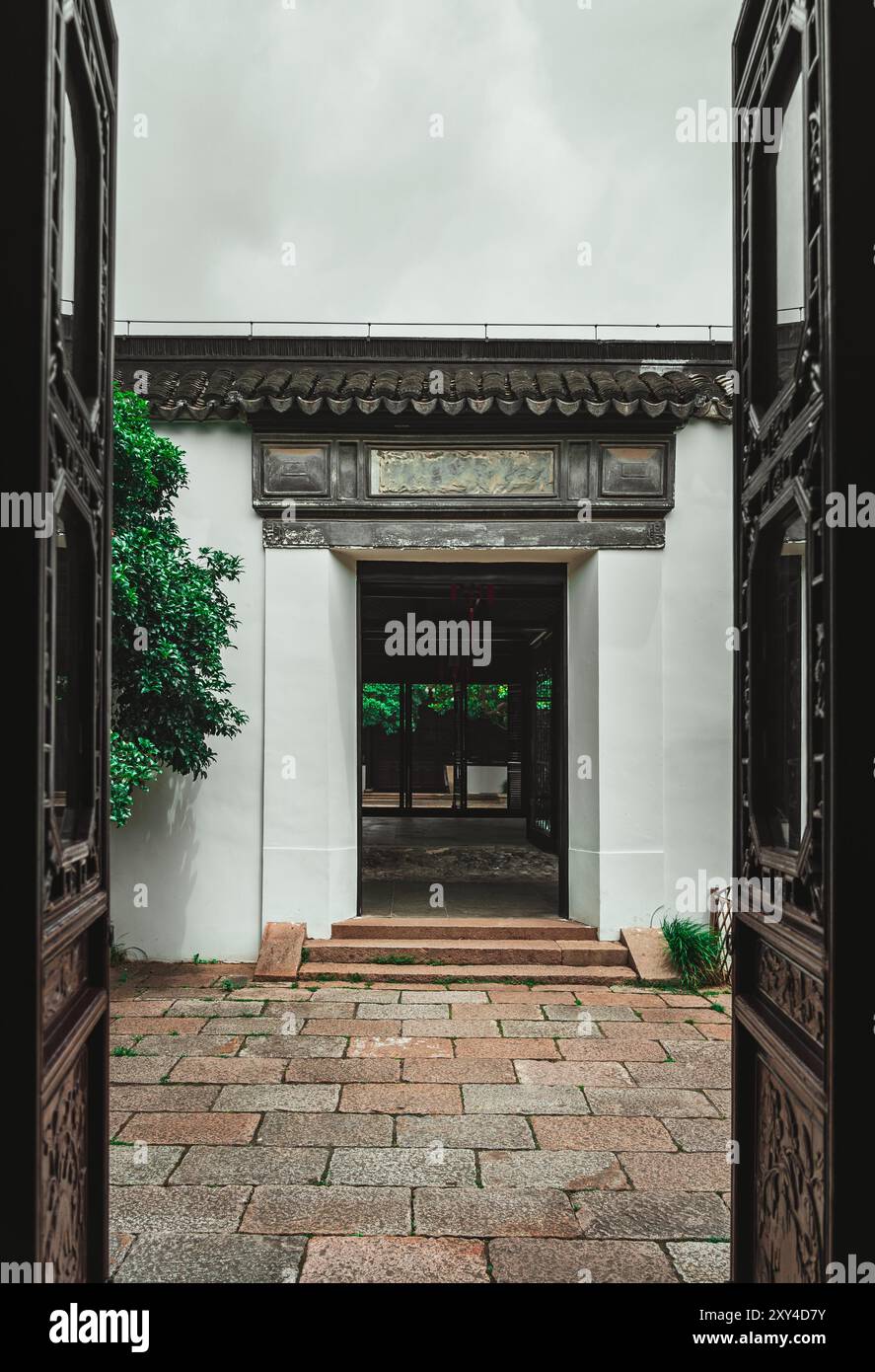 A doorway within a Chinese courtyard opens to reveal a view of a paved ...